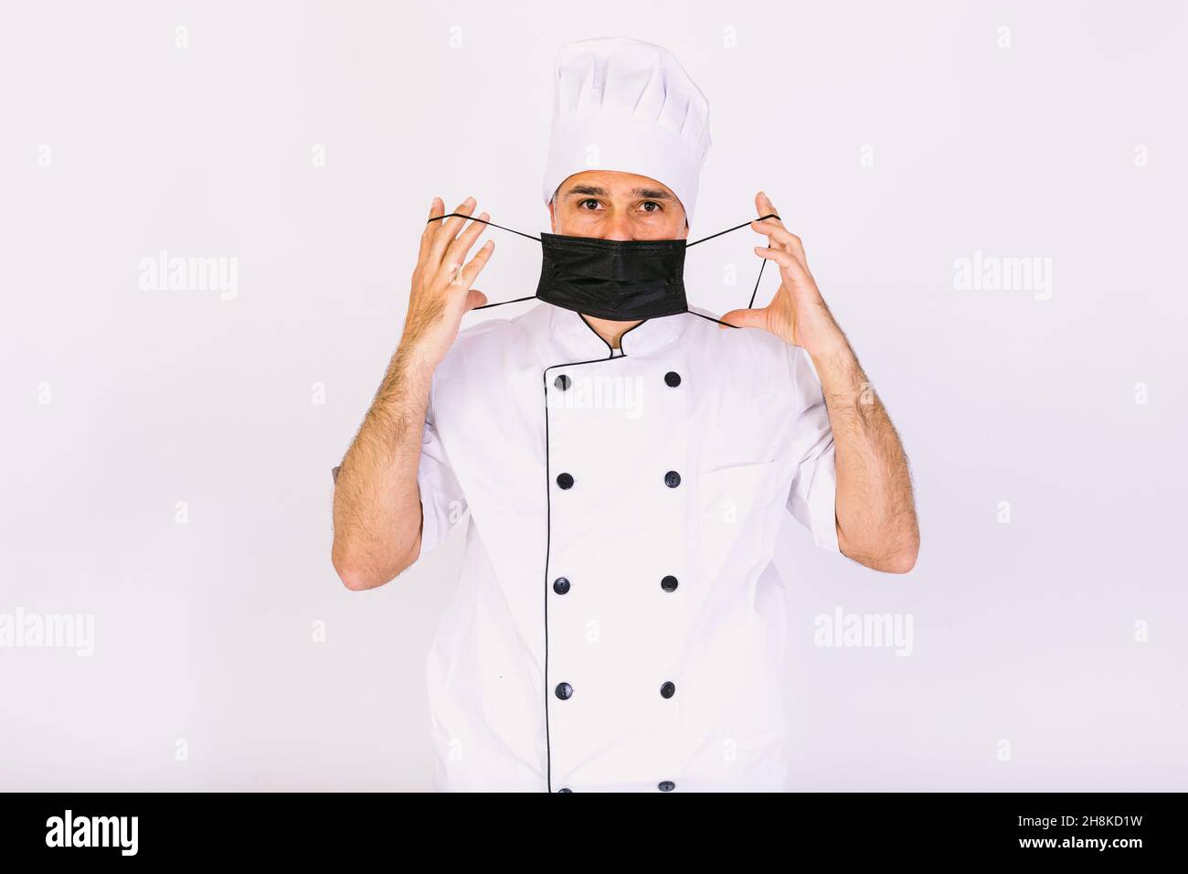 Chef cook wearing kitchen jacket and hat, putting on a black mask, on ...