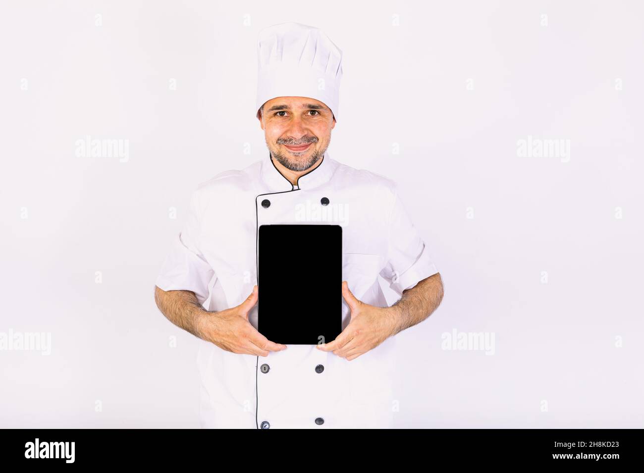 Chef cook wearing kitchen jacket and hat, holding a tablet, showing its ...