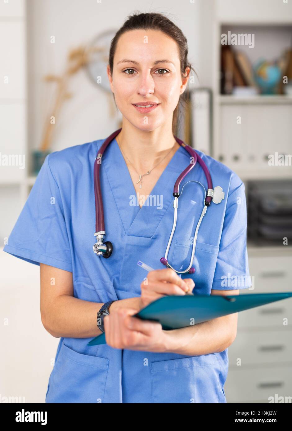 Positive woman doctor in formal wear standing with folder Stock Photo ...