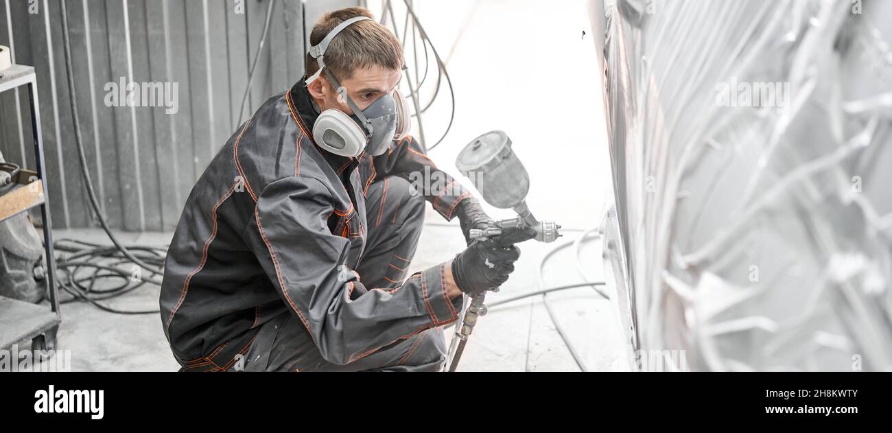 Painting the rear part of the car. Car painter wearing costume and ...