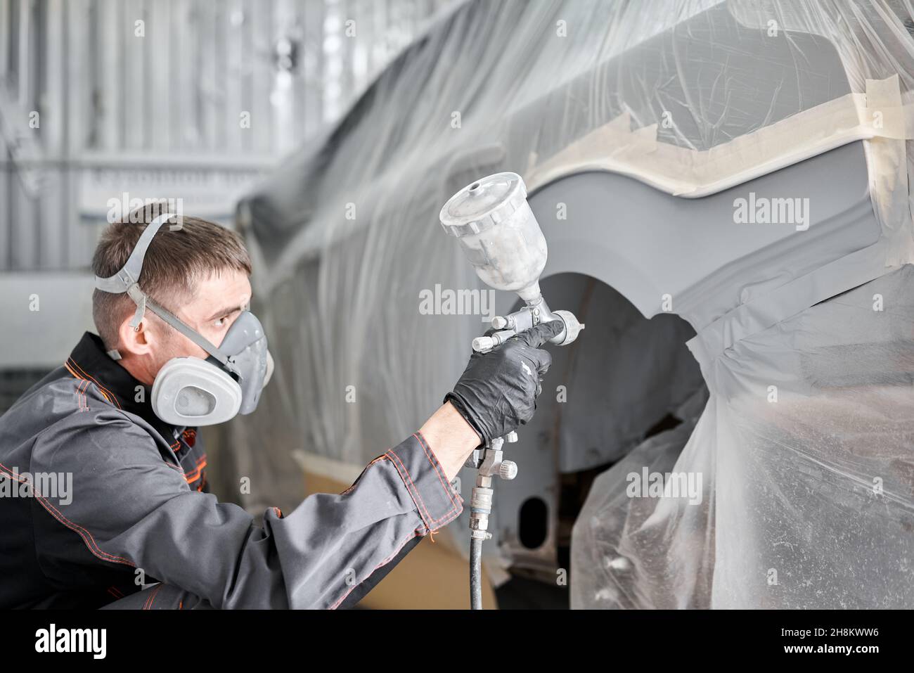 Painting the rear part of the car. Car painter wearing costume and ...
