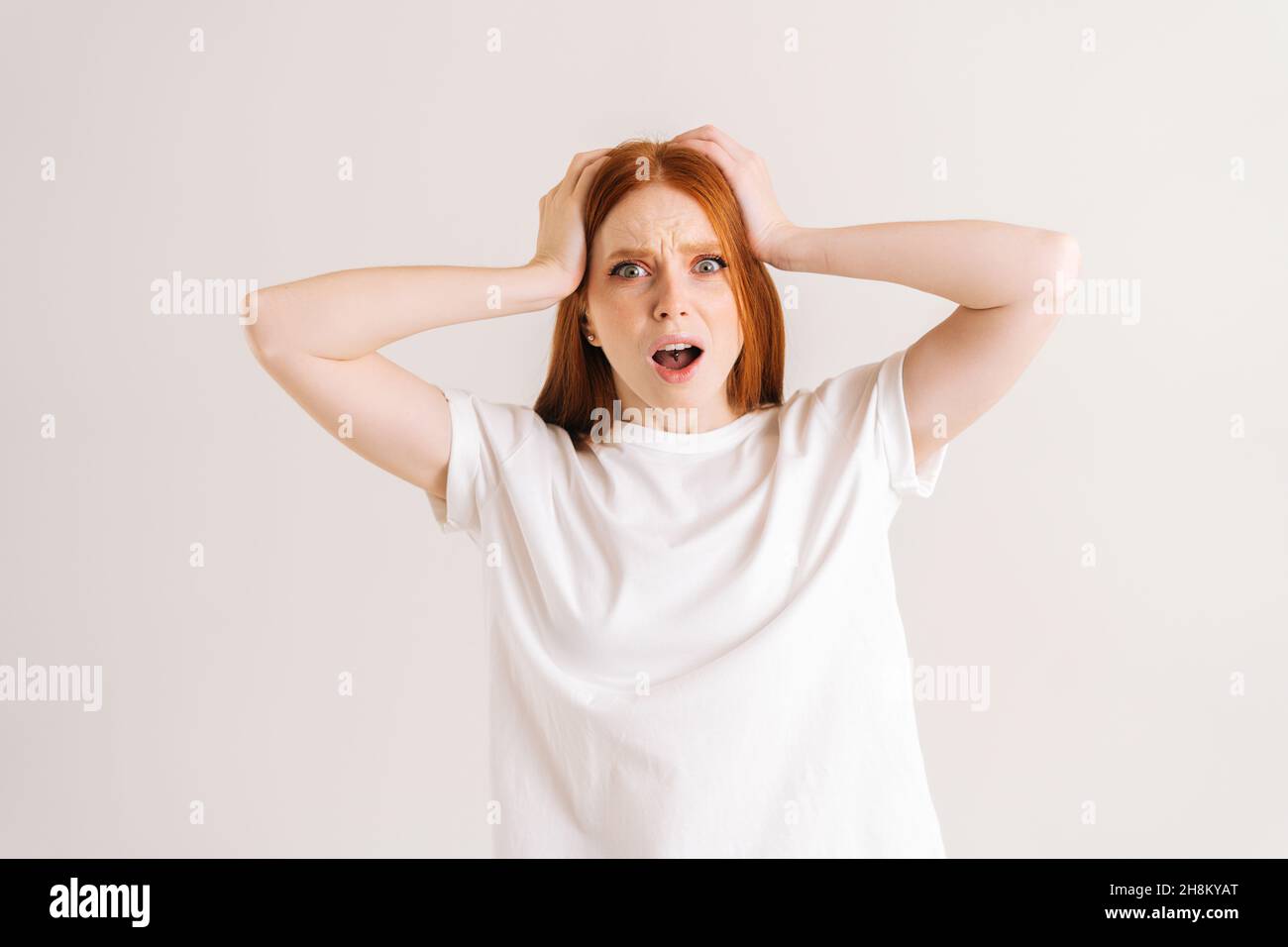 Studio portrait of confused scared young woman with hands on head ...