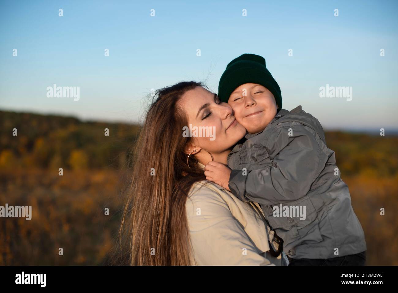 Little caucasian boy giving a hug to his happy smiling mother outdoors ...