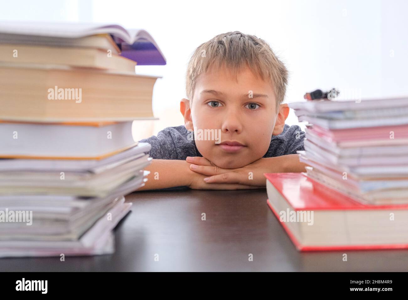 Teenage boy doing homework at home. Kid sitting among pile of books ...