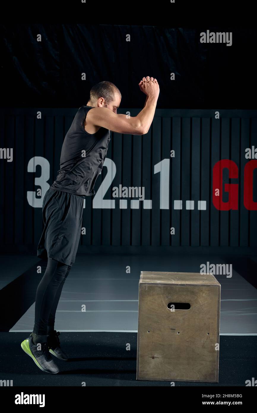 Fit young man jumping onto a box as part of exercise routine. Man doing ...