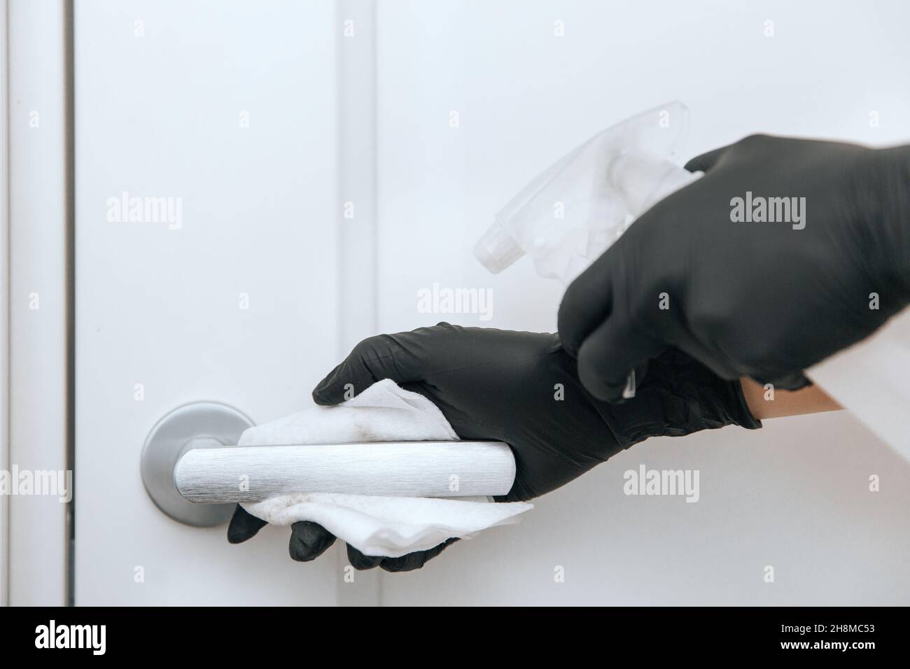 Cleaning door handle with dirty wipe in black gloves and sanitizer ...