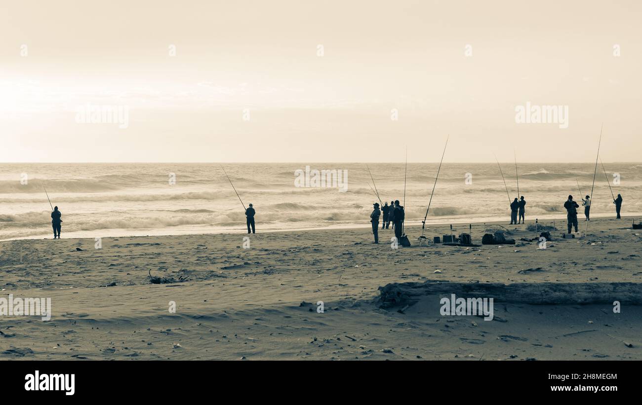 Fishing silhouetted in sepia tone unrecognizable fishermen by the beach ...