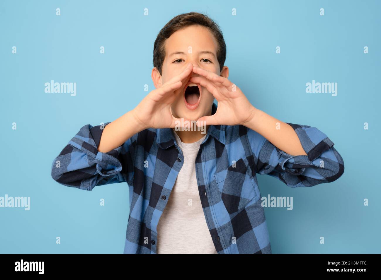 Boy wearing plaid shirt shouting making hand gesture on mouth isolated ...