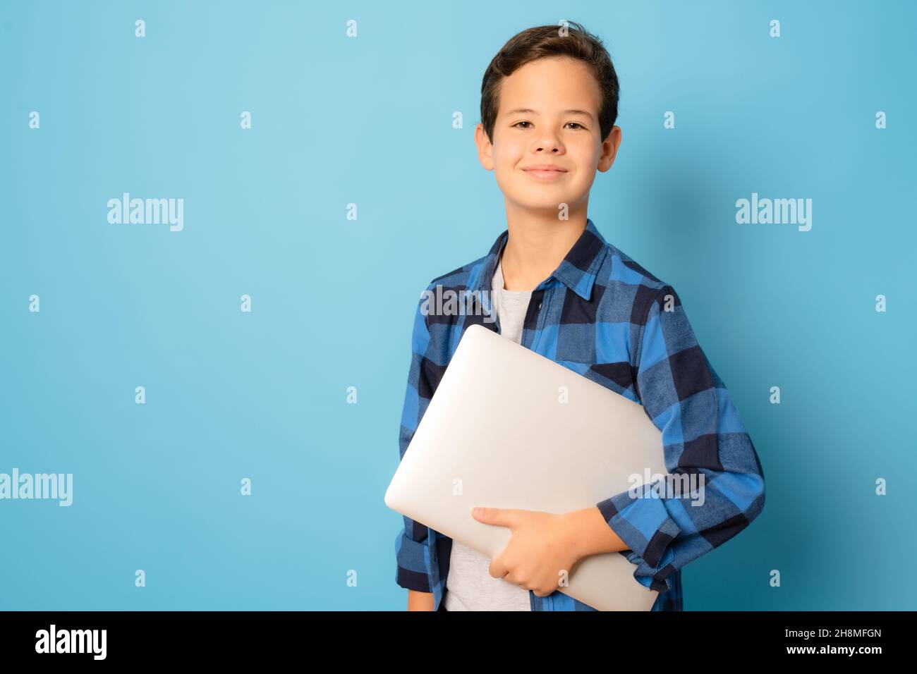 Cute kid boy in plaid shirt holding laptop computer standing over blue ...