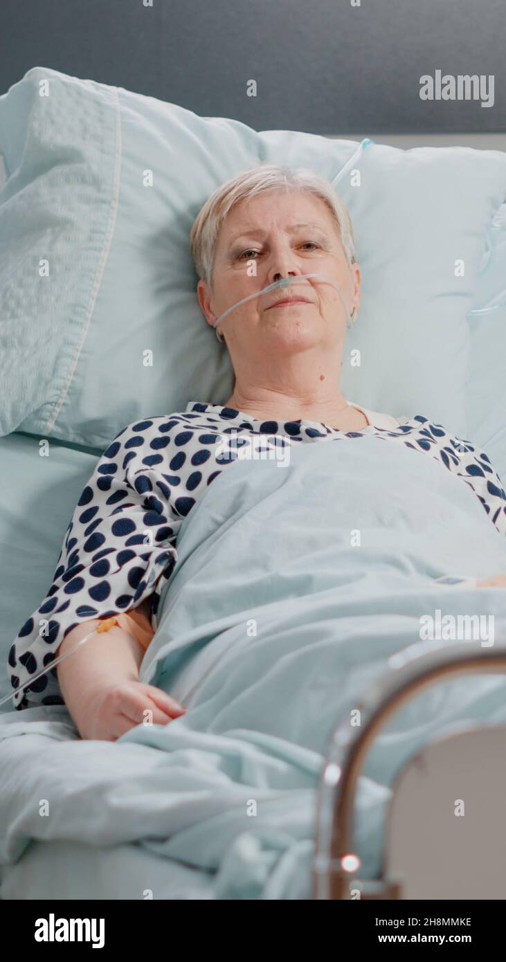 Portrait of sick patient laying in hospital ward bed, looking at camera ...