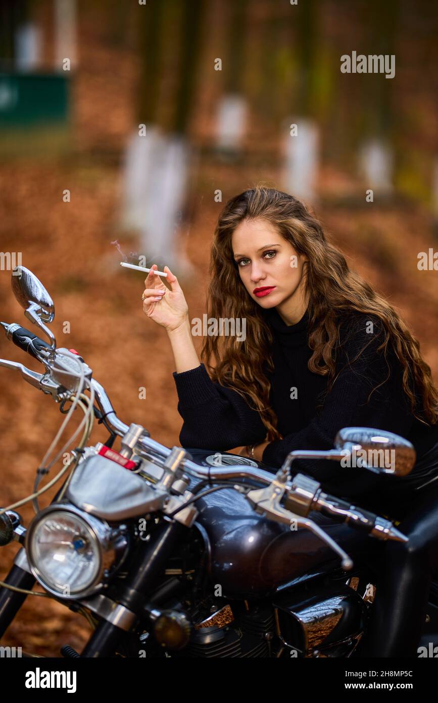 A beautiful long-haired woman smoking on a chopper motorcycle in autumn ...