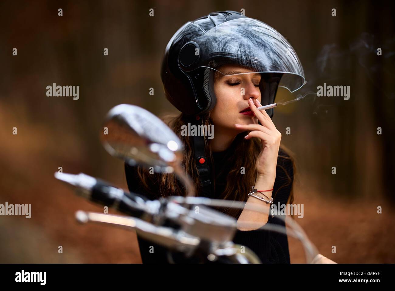 A beautiful long-haired woman smoking on a chopper motorcycle in autumn ...