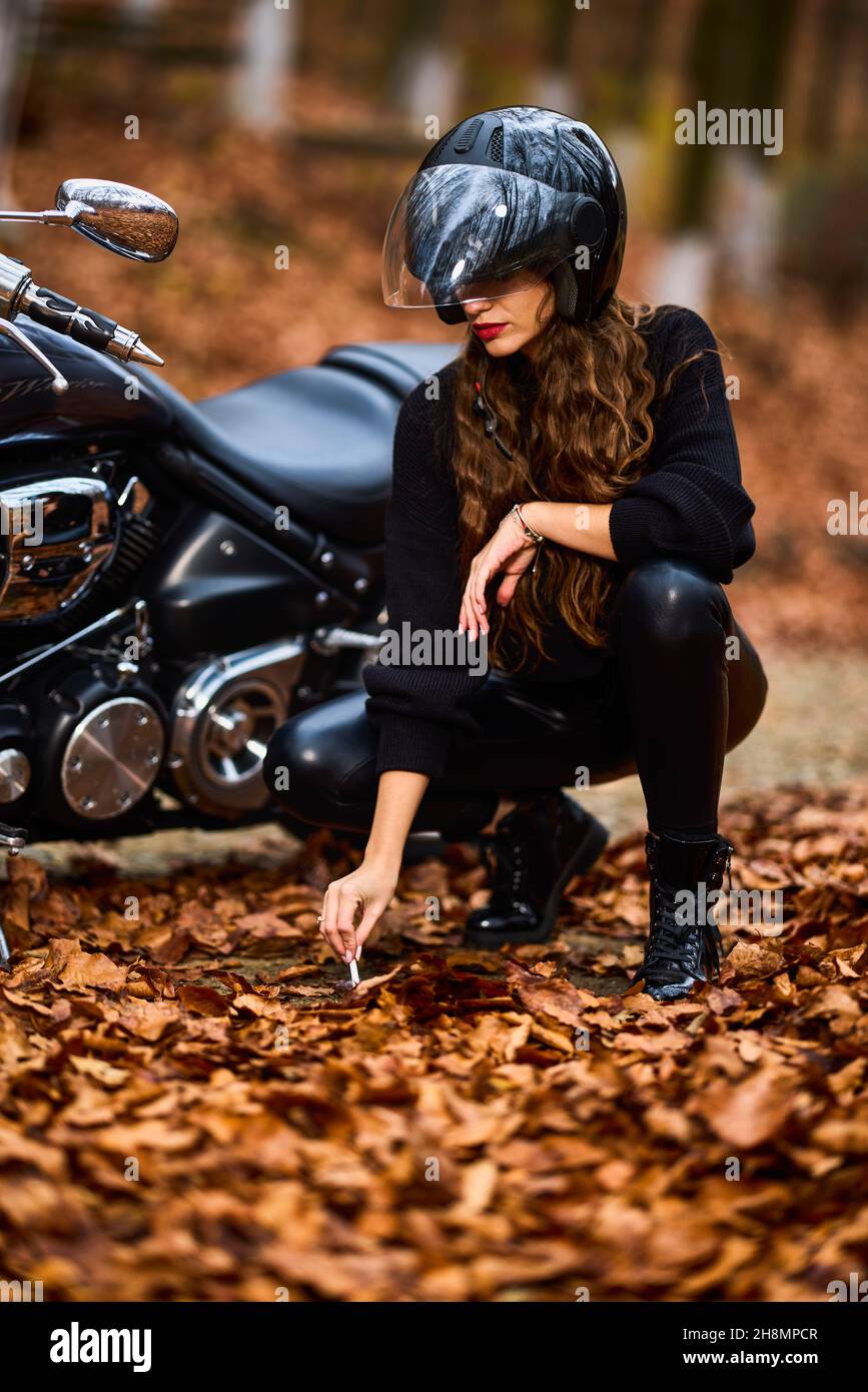 A beautiful long-haired woman smoking on a chopper motorcycle in autumn ...