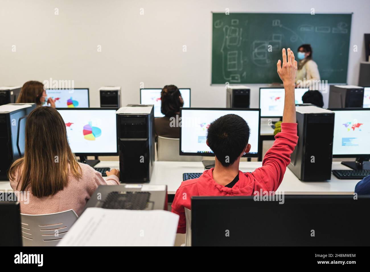 Young students using computers during business class wearing safety ...