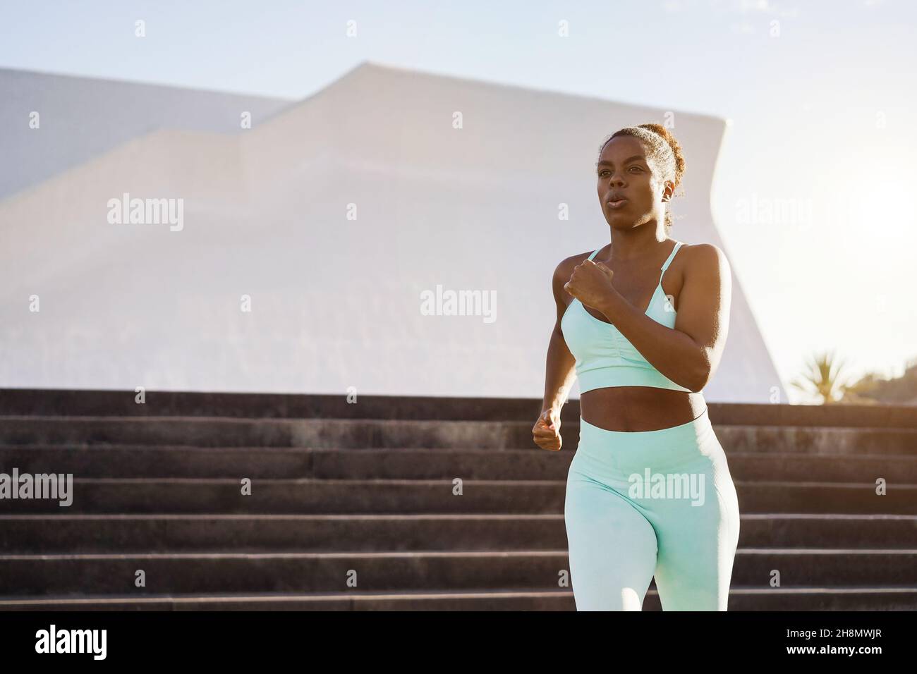 Fit african woman running outdoor in the city during sunset time ...