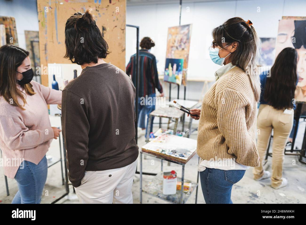 Young students painting inside art room class wearing safety masks ...