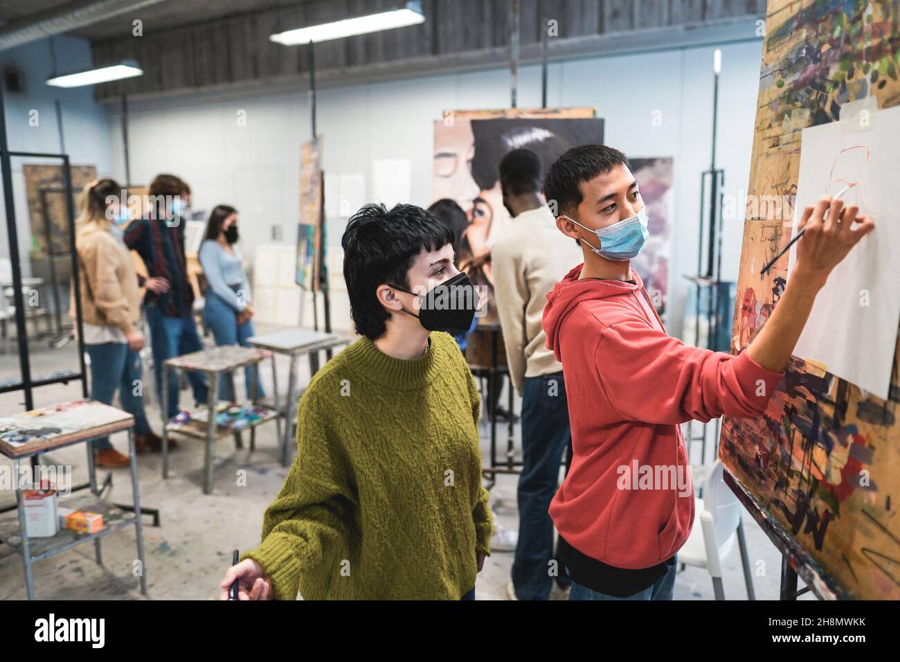 Multiracial students painting inside art room class wearing safety ...