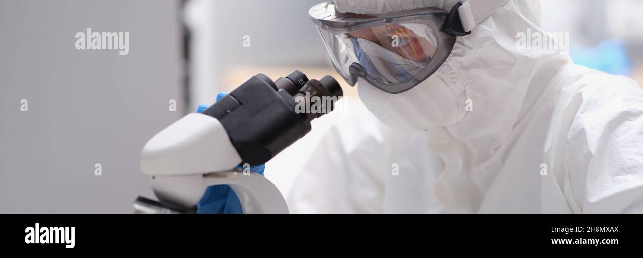 Scientist in protective suit and mask looks through microscope Stock ...