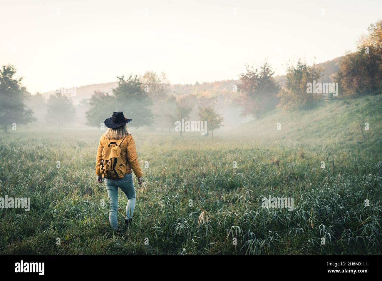 Hiking at autumn nature. Woman with backpack and hat walking in grass ...