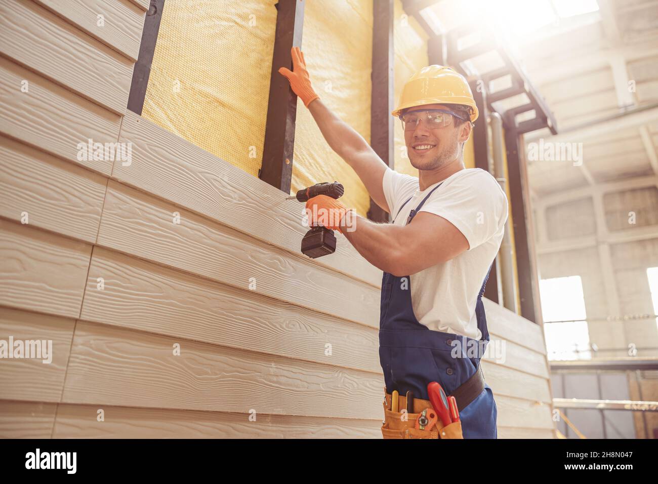 Cheerful builder using cordless electric drill at construction site ...