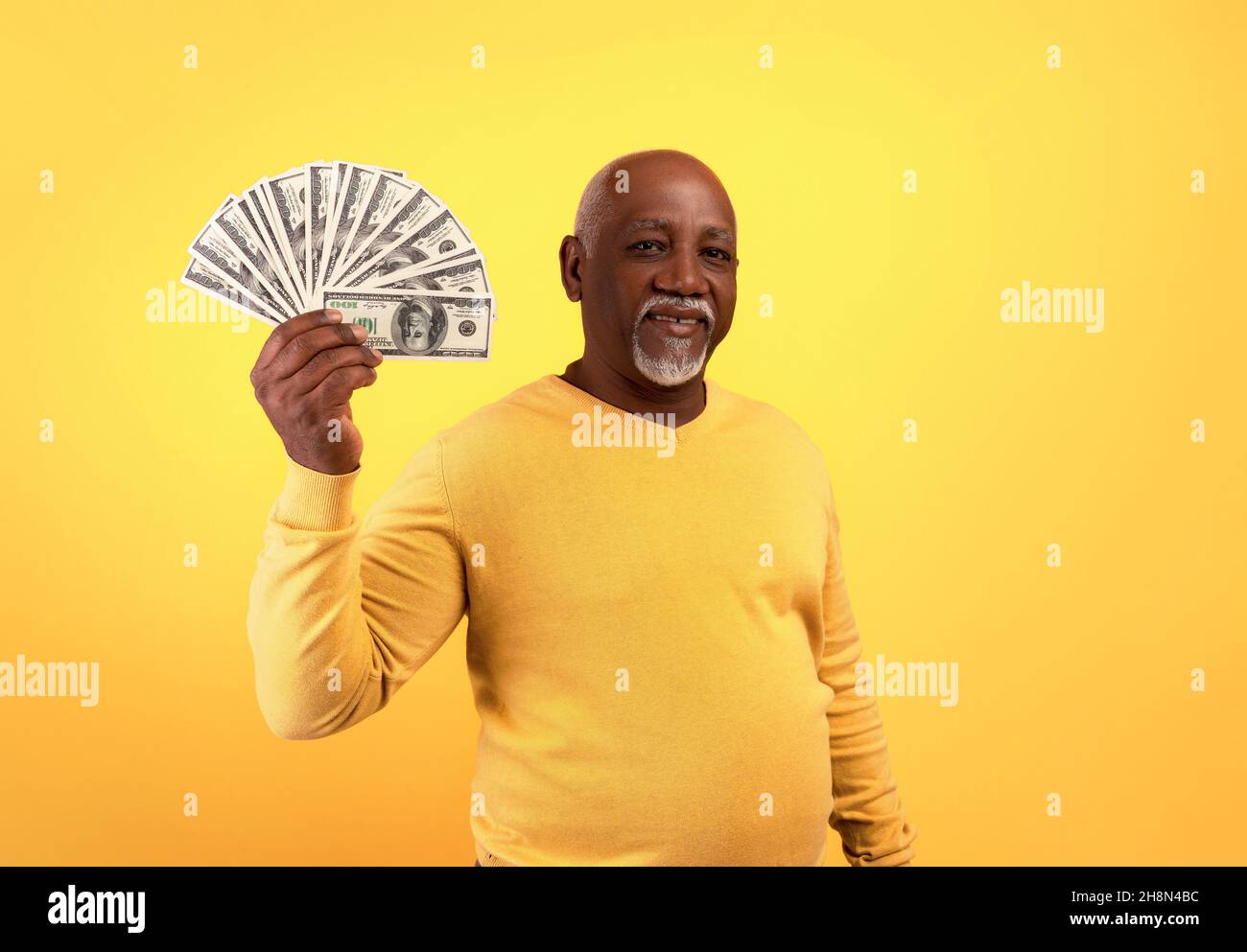 Portrait of smiling senior black man holding lots of money on orange ...