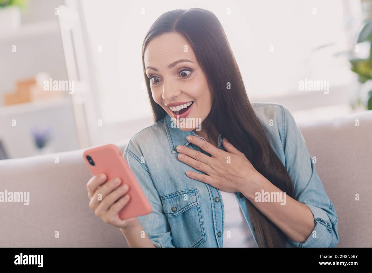 Portrait of attractive cheerful amazed long-haired woman using gadget ...