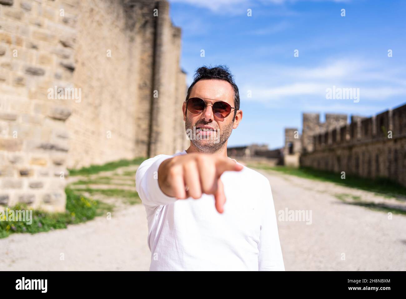 Man with sunglasses pointing forward while standing next to a medieval ...