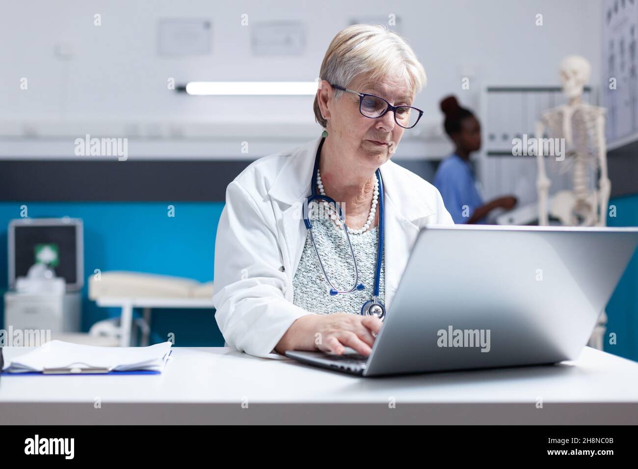 Portrait of physician with stethoscope using laptop to work on ...