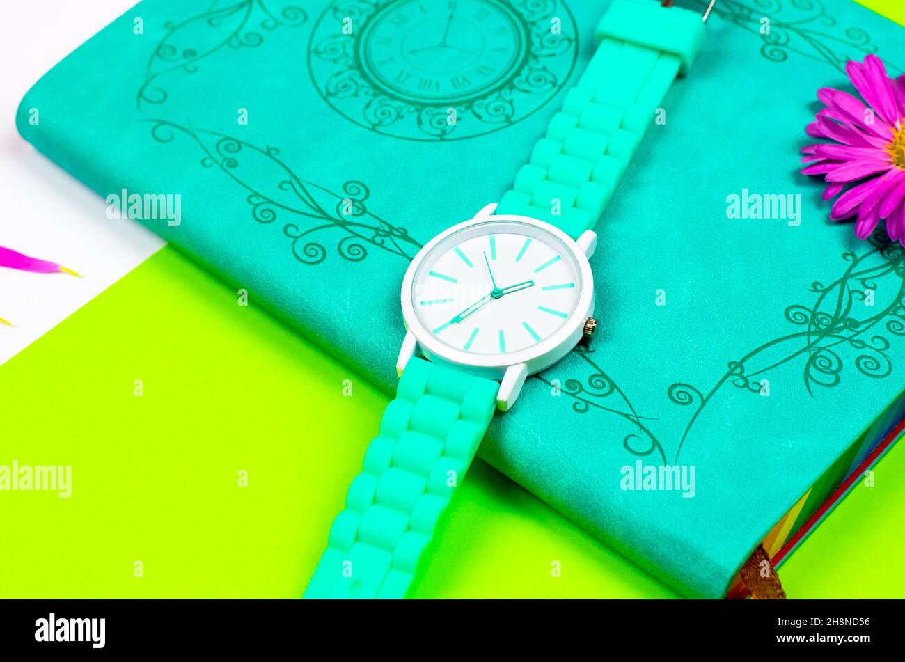 A mint-colored watch is on a notebook. Notepad and clock with flower ...