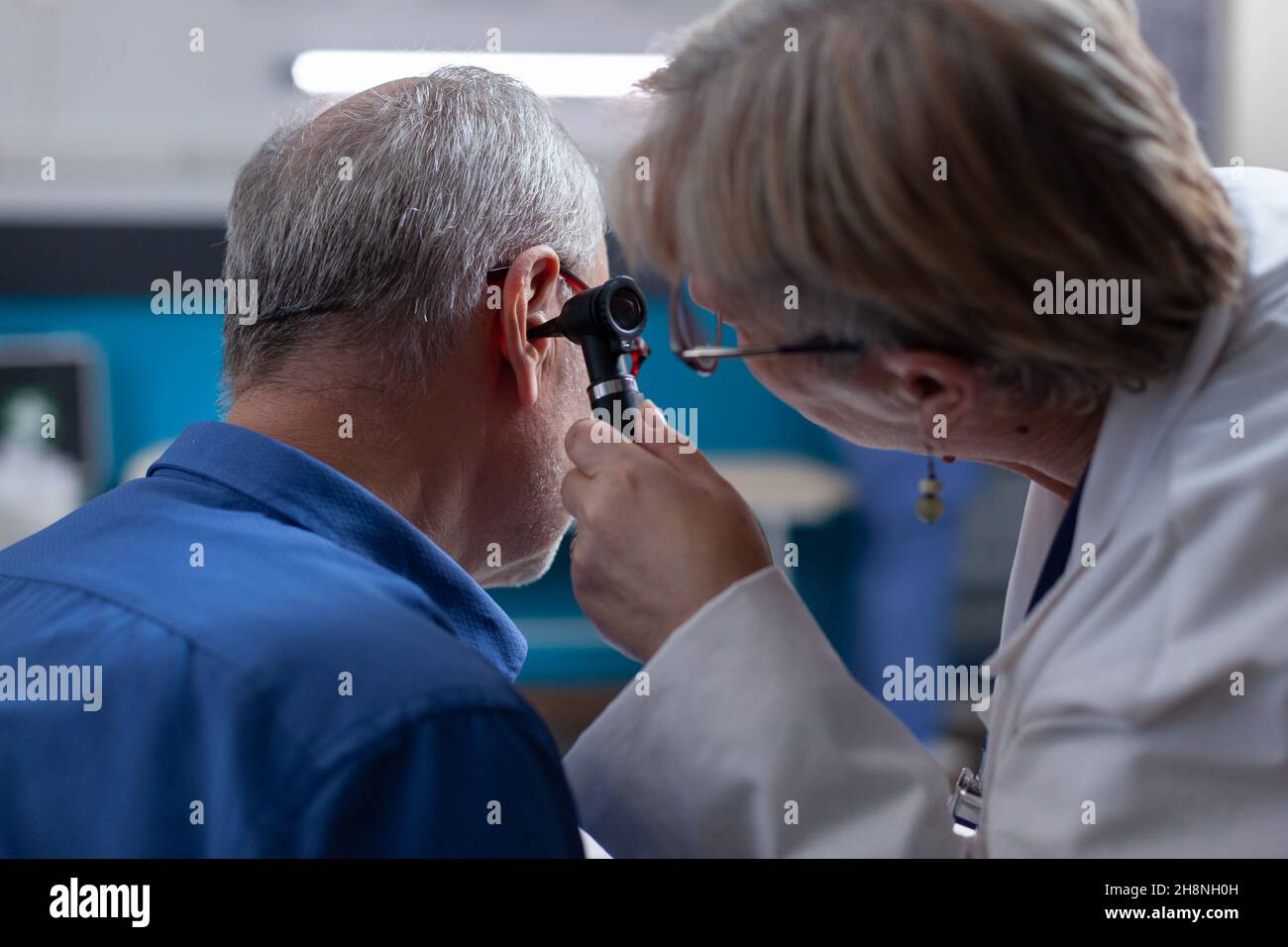 Woman doctor holding otoscope to do ear consultation for old man at ...
