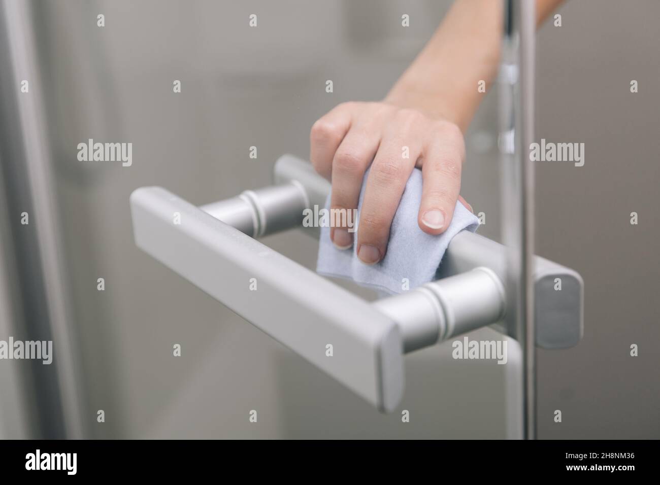 Cleaning glass door handles with an antiseptic wet wipe. Woman hand ...