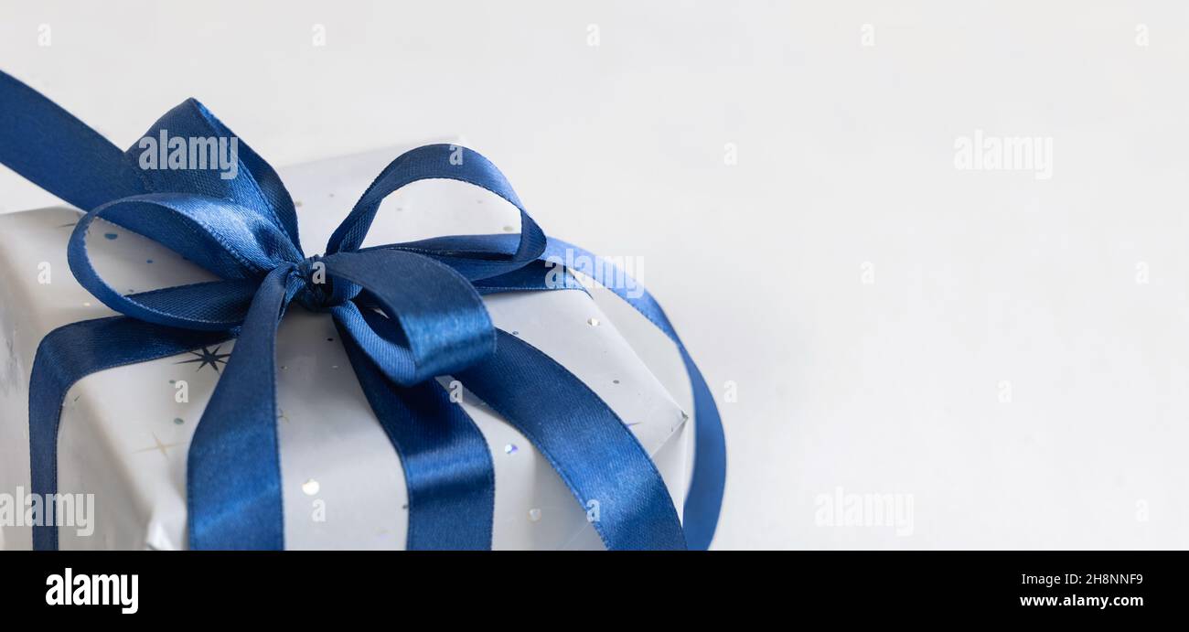Grey Wrapped Christmas present with a blue ribbon bow on grey close up ...