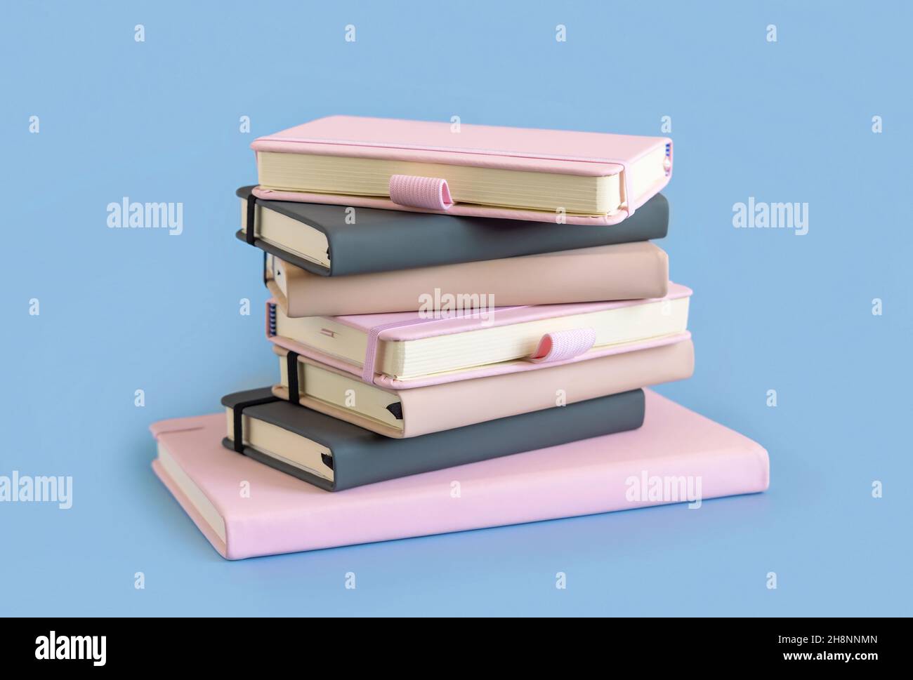 Stack of pink, beige and grey notebooks on light blue closeup. Textbook ...