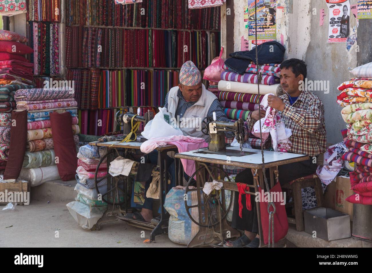 Two tailors sewing on foot-treadle sewing machines in an outdoor shop ...