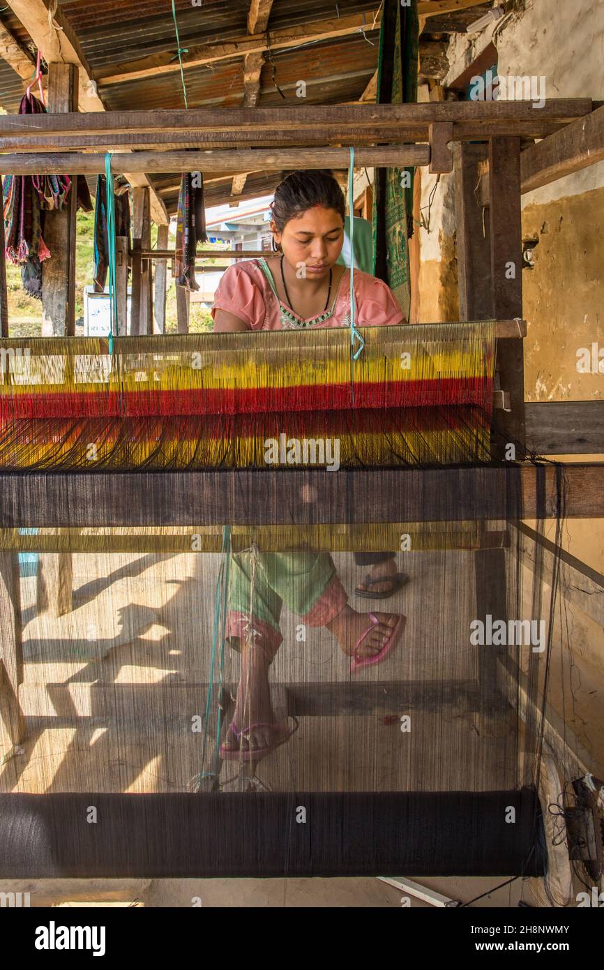 A young Nepali woman in weaving fabric on a wooden foot loom in Dhampus ...