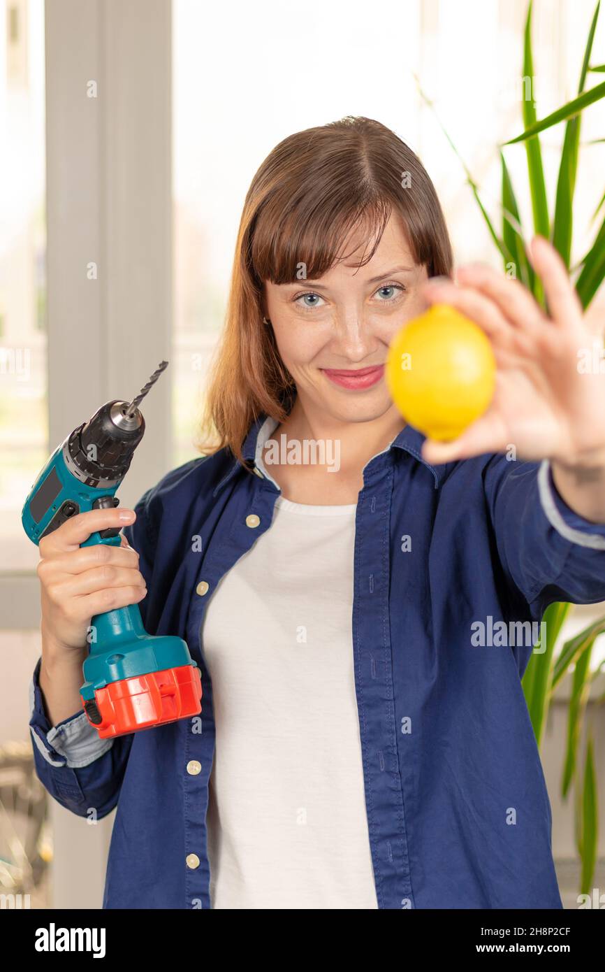 A young pretty woman in a blue shirt holds a screwdriver with a drill ...