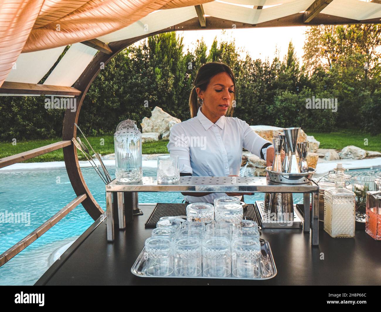 Female bartender preparing cocktails near an outdoor pool venue ...