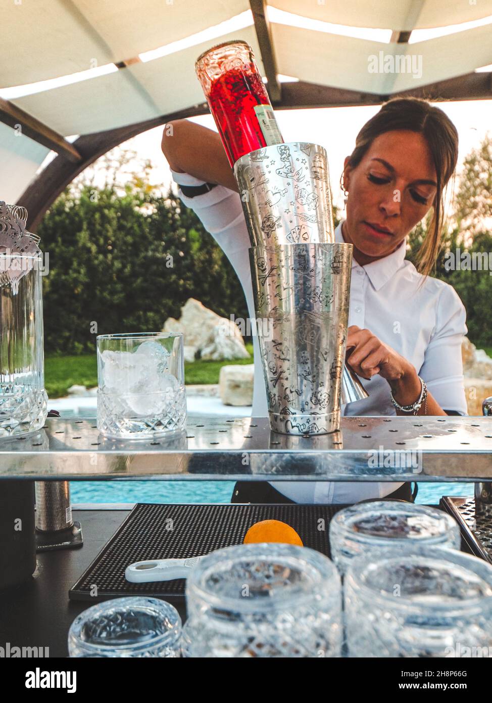 Female bartender preparing cocktails near an outdoor pool venue ...