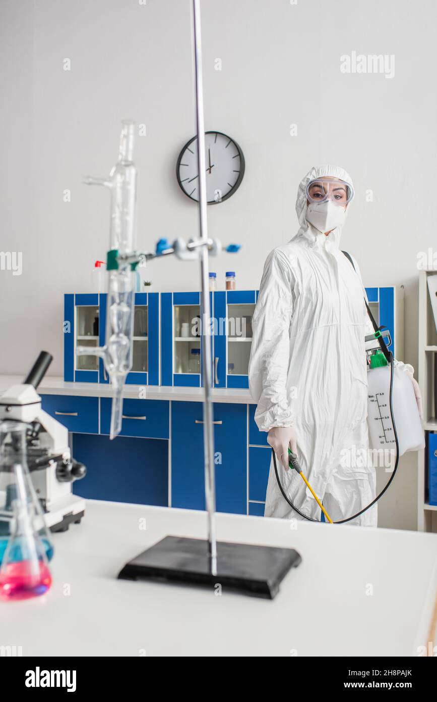 doctor in hazmat suit holding sprayer while looking at camera in lab ...
