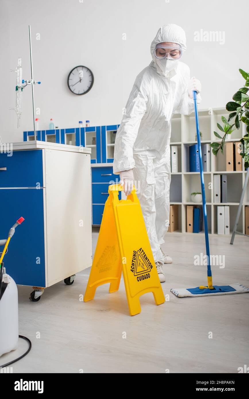 doctor in hazmat suit holding mop and attention board while cleaning ...