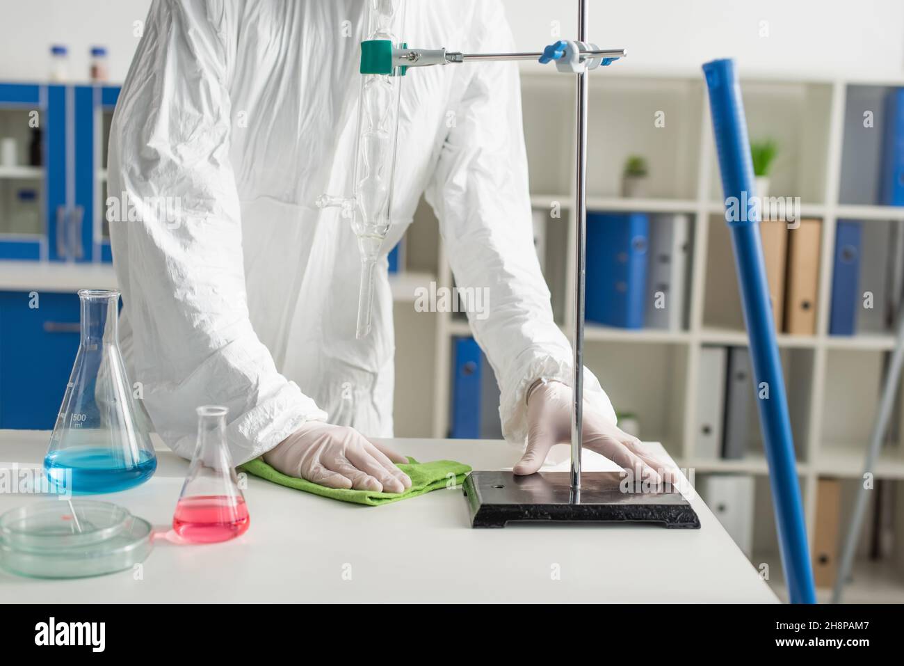 partial view of doctor in hazmat suit wiping desk while making ...