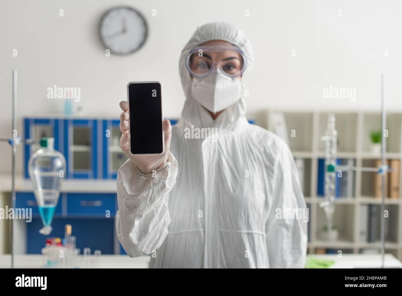 blurred doctor in hazmat suit holding mobile phone with blank screen in ...