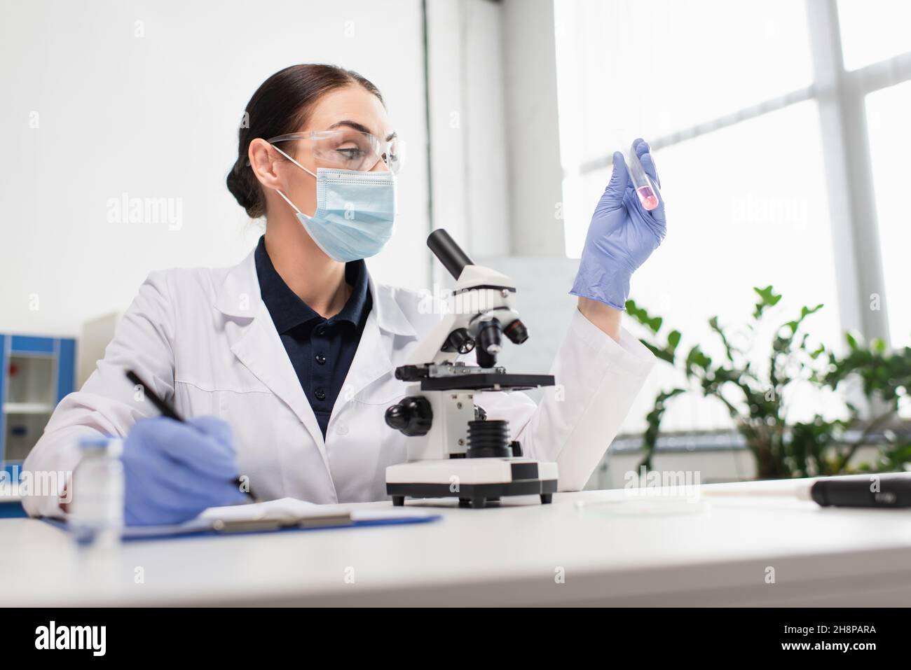 Scientist in white coat and goggles holding test tube and writing on ...
