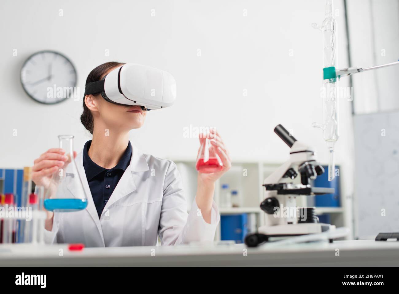 Scientist in vr headset holding flasks while working near microscope ...