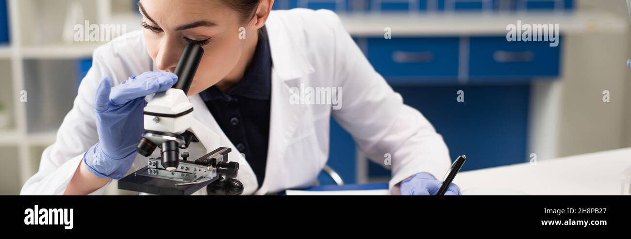 Scientist holding pen and using microscope in lab, banner Stock Photo ...