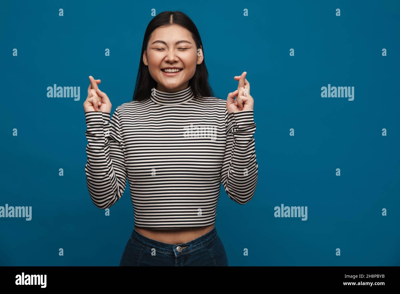 Portrait of a happy casual young asian woman standing over blue wall ...