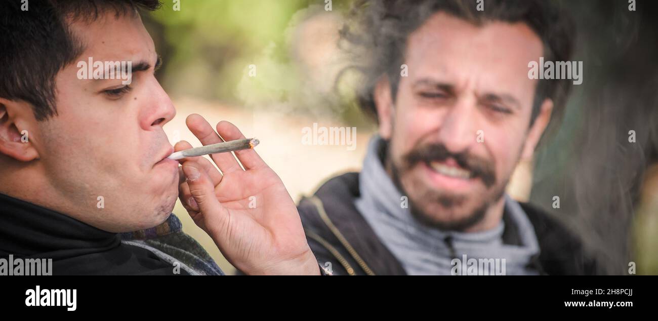 Two young friends smoking cannabis marijuana ganja or hashish joint in ...