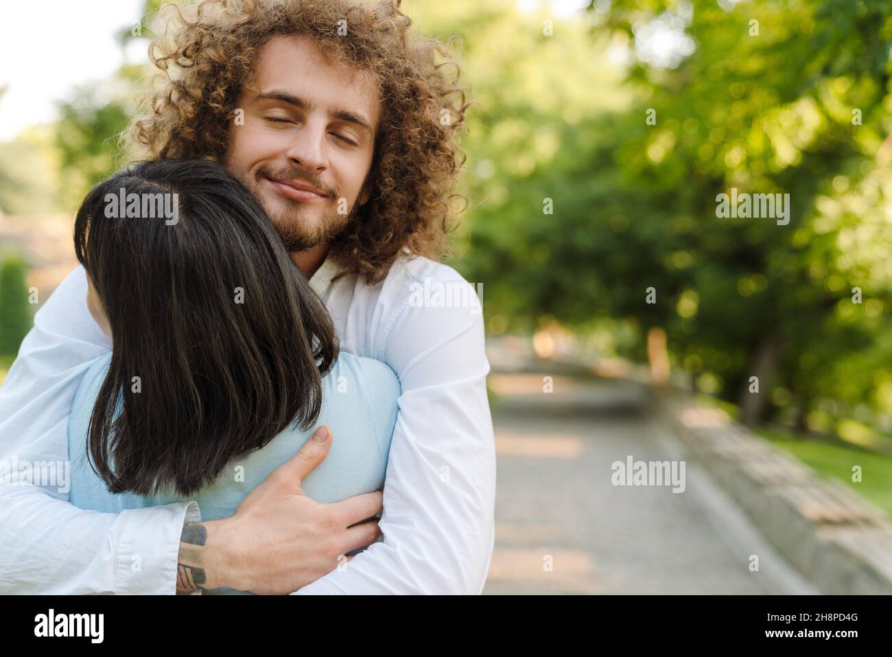 Happy young multiethnic couple cuddling embracing together in the green ...