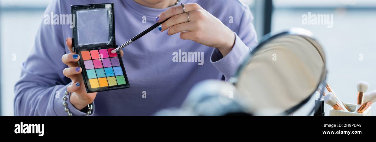 Cropped view of transgender person holding eye shadows and cosmetic ...