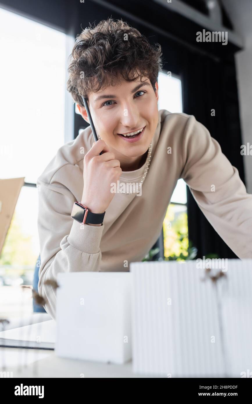 transgender person holding pen near blurred model of building in office ...
